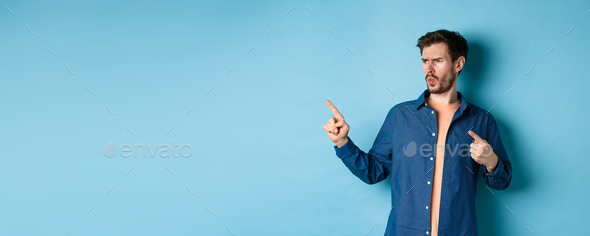 Confused and annoyed guy pointing and looking left at empty space with ...