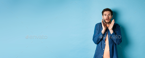 Shocked and scared young man standing in stupor, raising hands up and ...