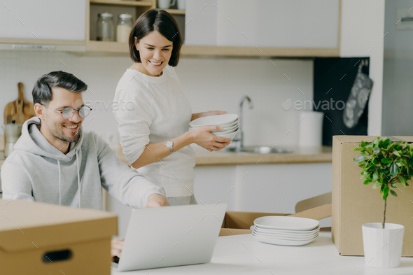 Caring brunette woman holds pile of plates, unpacks personal belongings ...