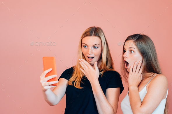 shocked young girls using a smartphone against a pink background Stock ...