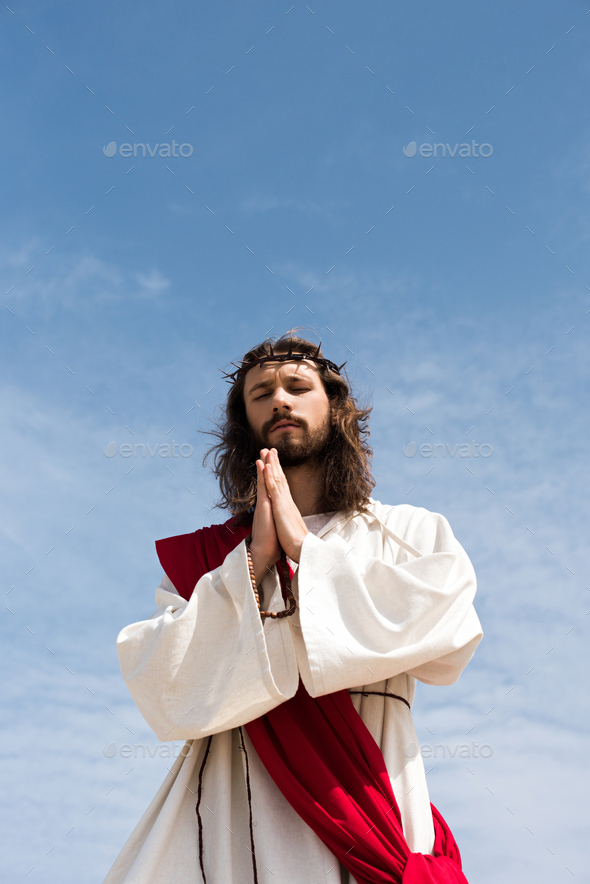 low angle view of Jesus in robe, red sash and crown of thorns holding ...