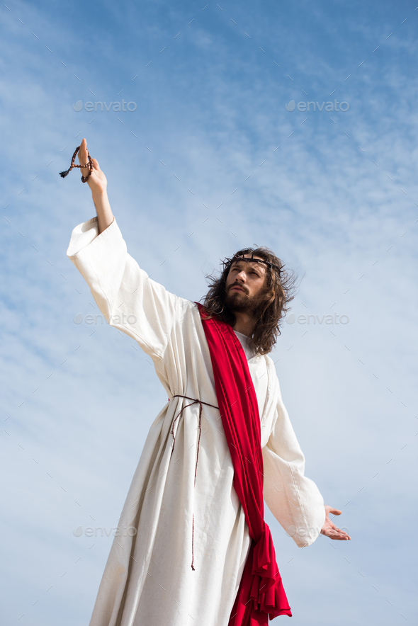 low angle view of Jesus in robe, red sash and crown of thorns holding ...