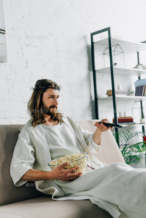 serious Jesus in crown of thorns watching tv and sitting with bowl of ...