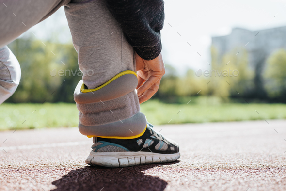 Close-up of female runner using fitness leg weights while exercising on ...