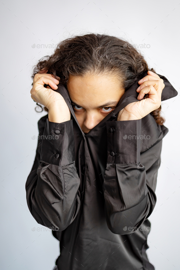 African teen girl hiding face under the clothes. She is pulling a shirt ...