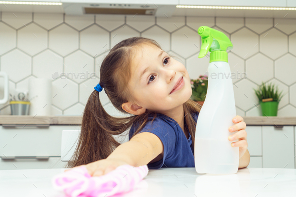 Nice little girl with detergent sprayer and household rag wipe table ...