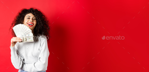 Successful young woman waiving dollar bills and smiling pleased. Rich ...