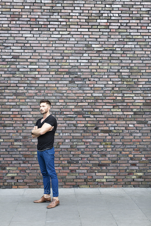 Serious man standing at brick wall Stock Photo by westend61 | PhotoDune