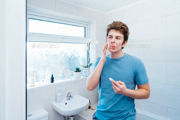 Concentrated caucasian teenage boy with acne problem take care his face ...