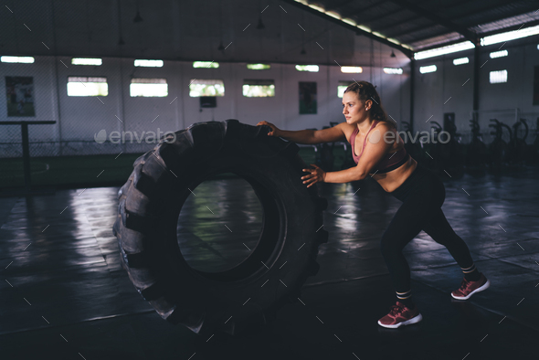 Strong bodybuilder in tracksuit using wheel tire during weightlifting ...