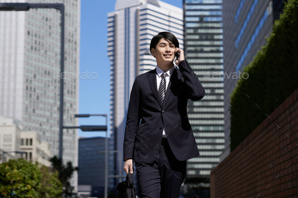 A Japanese male businessman making a phone call in an office district ...