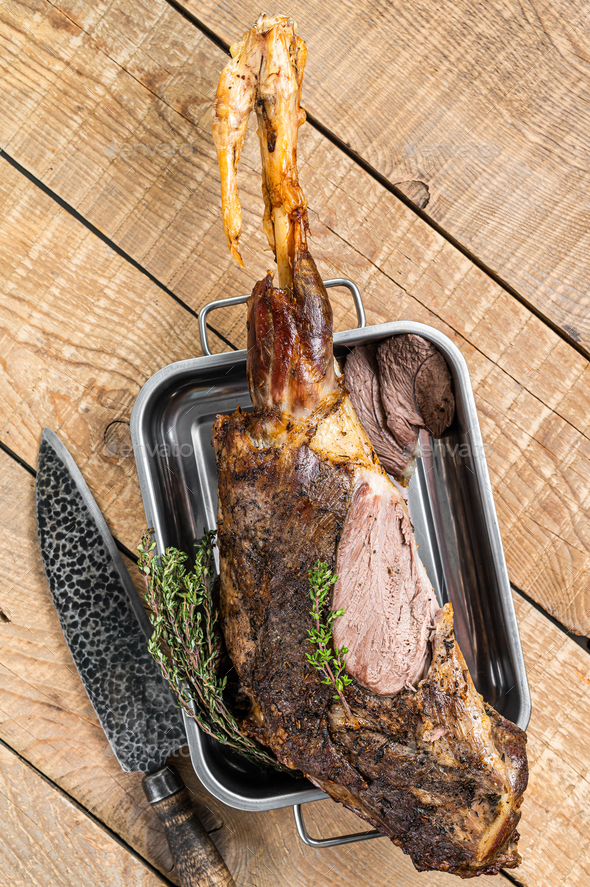 Whole oven roasted goat leg meat with thyme in a steel tray. Wooden ...