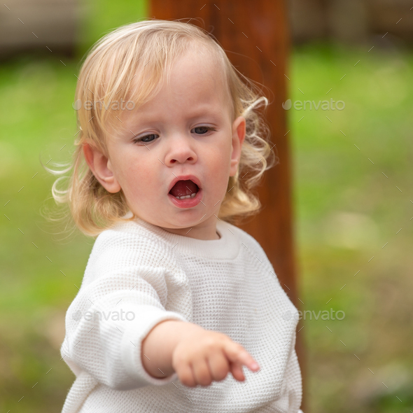 Pointing child sitting outdoors on a nice day. Cute blonde kid sitting ...