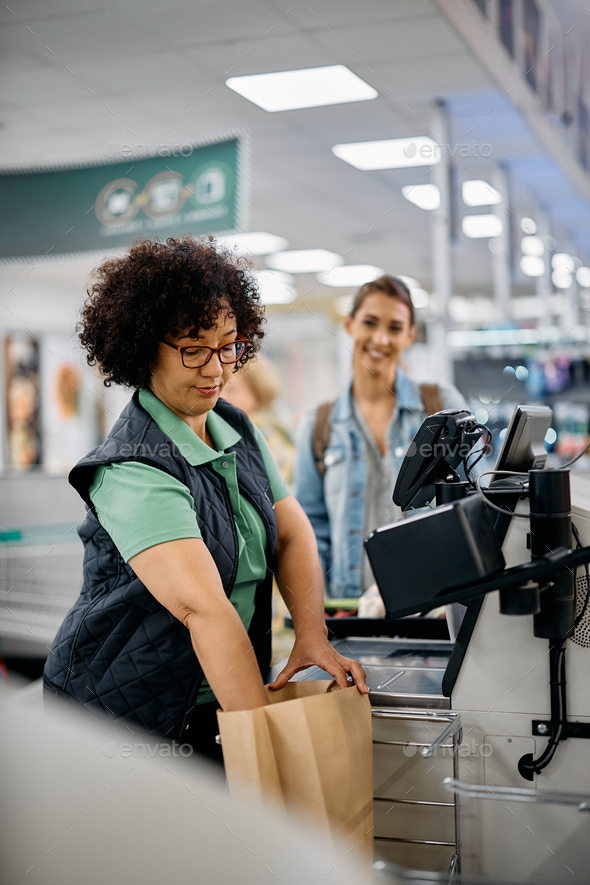 Supermarket worker assisting her customer with using paper bag at self ...