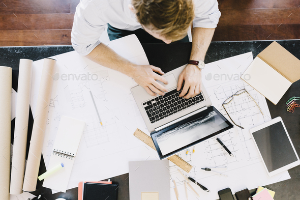 Man using laptop next to construction plan at desk, top view Stock ...