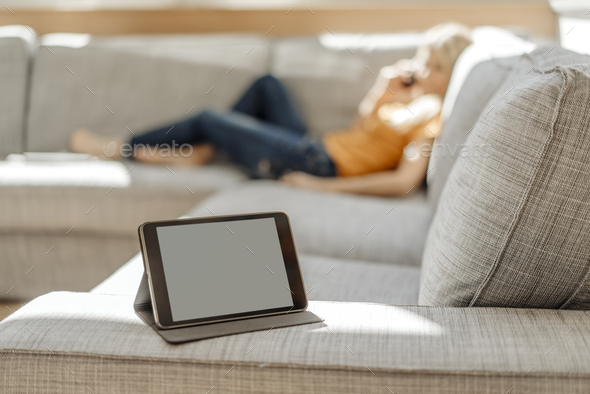 Tablet on couch with relaxed woman in background Stock Photo by westend61