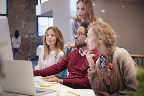 Colleagues looking over shoulder of young man working in modern office ...