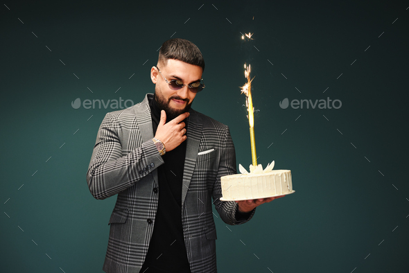 Handsome young man holding cake in his hand with lighted sparkling ...