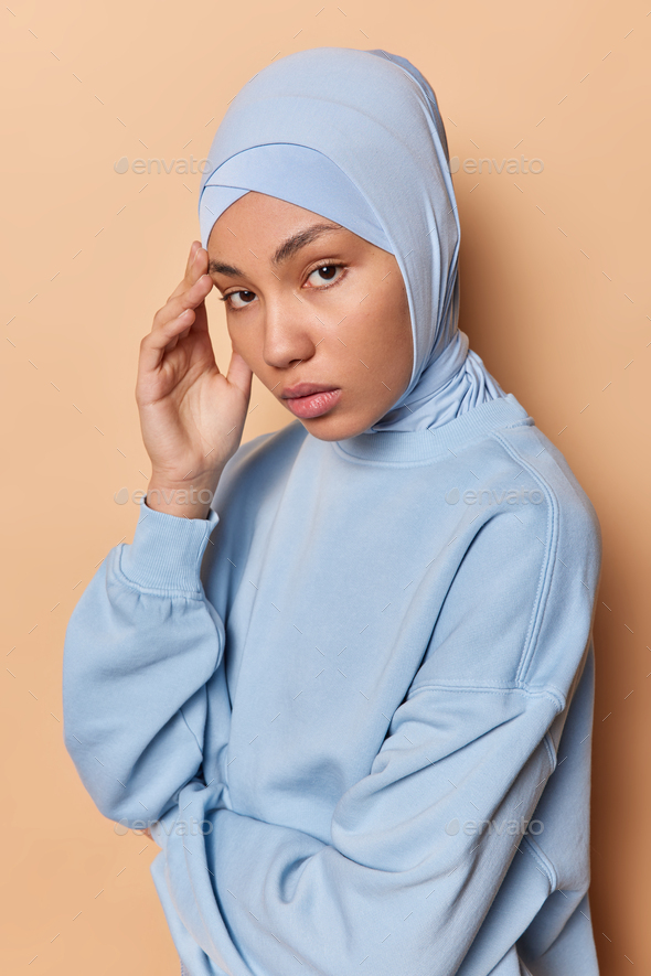 Serious Muslim woman touches face looks directly at camera has calm ...