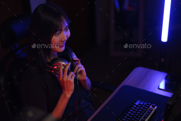 Female cyber hacker gamer in headphone around neck watching video games ...