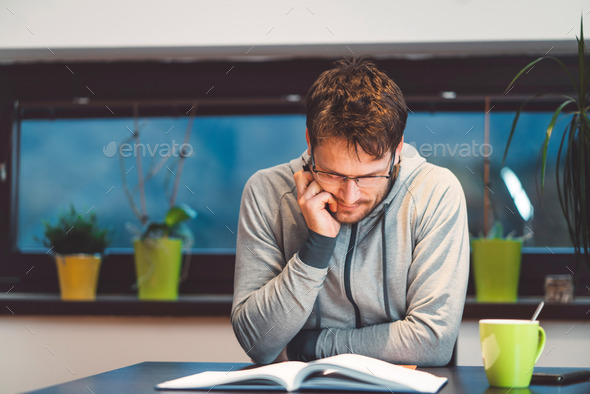 Waist up man sitting by the table in the evening studying at home ...