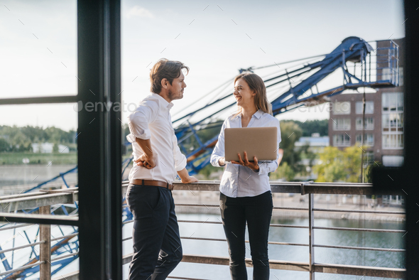Business people standing on balcony, discussing, using laptop Stock ...