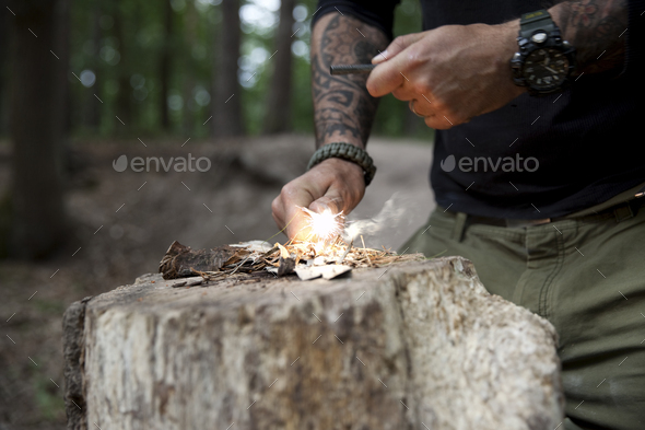 Man igniting a fire on tree stump in the forest Stock Photo by westend61