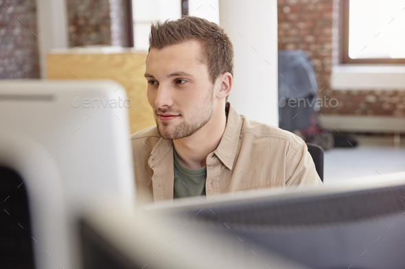 Young man sitting in office using computer Stock Photo by westend61