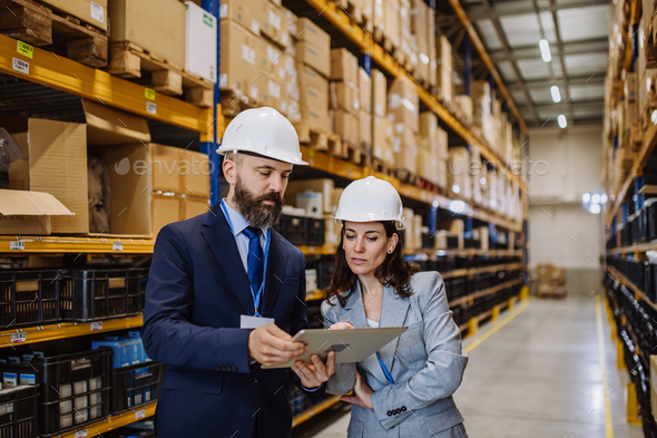 Managers in suit controlling goods in a waehouse. Stock Photo by halfpoint