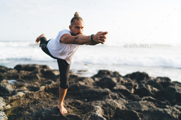 Pumped up male yogi recreating doing balance yoga poses feeling inner ...