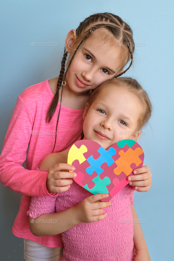 Sisters with pigtails look with smile at the camera holding the autism ...