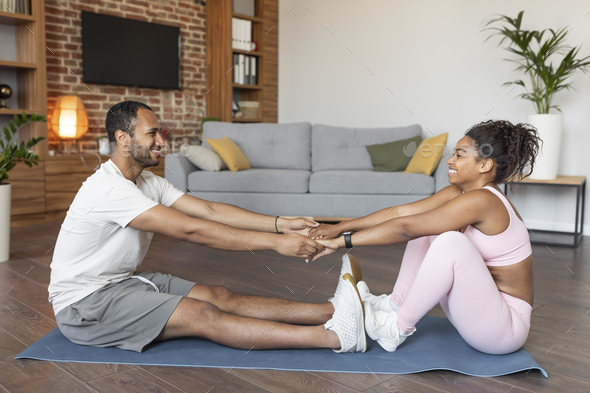 Cheerful young black couple in sportswear do muscle exercises for legs ...