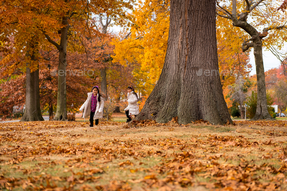 Two young asian girls running around big tree Stock Photo by naokawa