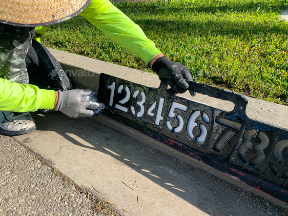 City worker painting address on street curbs using stencil numbers ...