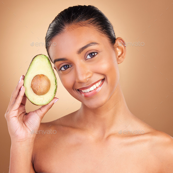 Portrait, beauty and avocado with a model woman in studio on a brown ...