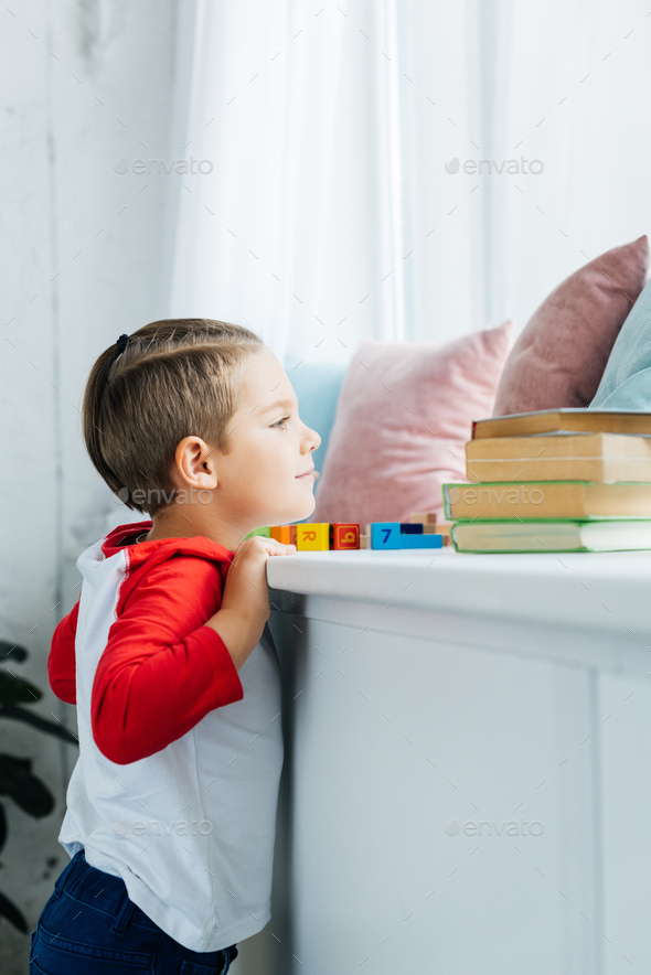 side view of child standing at surface with books and colorful blocks ...