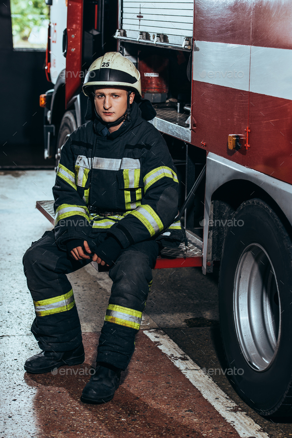 male firefighter in uniform and helmet at fire truck at fire department ...