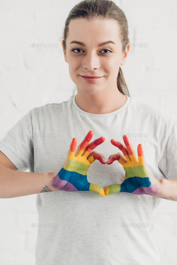 smiling young transgender woman making heart sign with hands in colors ...