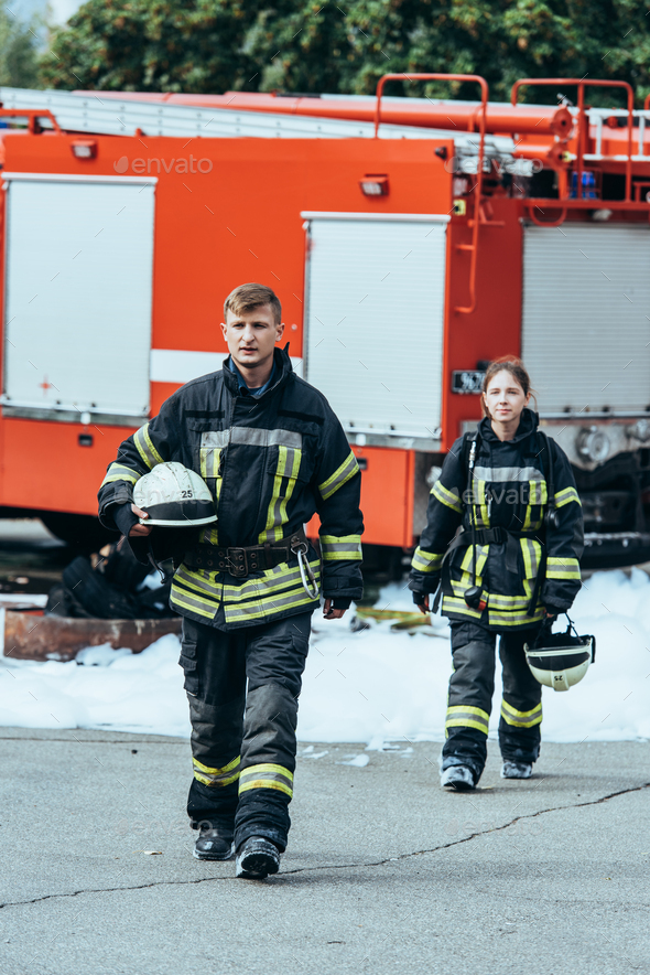 firefighters in fireproof uniform with helmets walking on street with ...