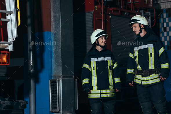 smiling firefighters in protective uniform and helmets looking at each ...