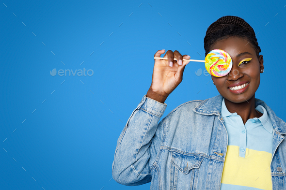 Playful young black woman with candy posing on blue Stock Photo by ...