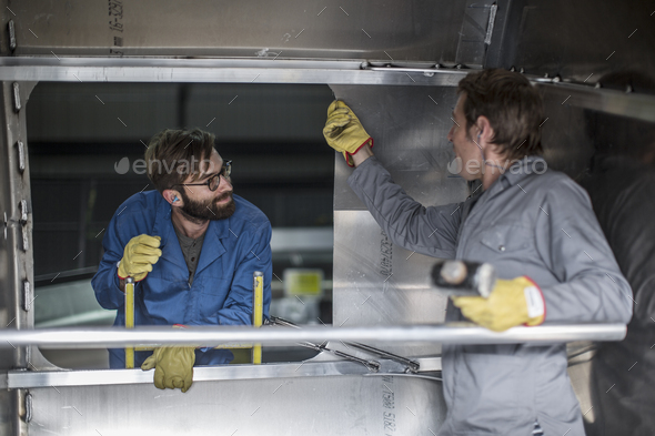 Two men discussing inside of steel container in factory Stock Photo by ...
