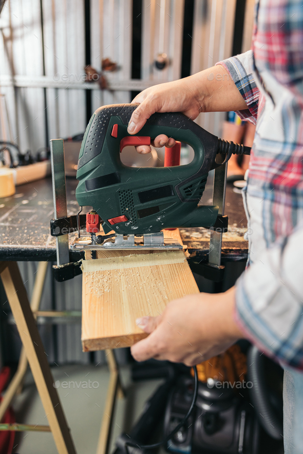 Carpenter cutting wood with an electric jigsaw, side view Stock Photo ...