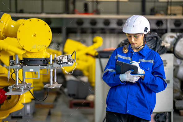 Engineer inspecting automatic AI robot arm and machines in factory ...