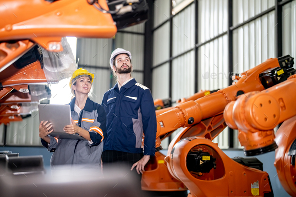 Engineer inspecting automatic AI robot arm and machines in factory ...