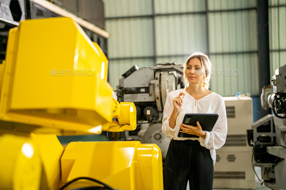 Engineer inspecting automatic AI robot arm and machines in factory ...