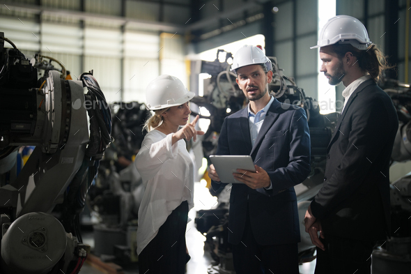 Engineer inspecting automatic AI robot arm and machines in factory ...