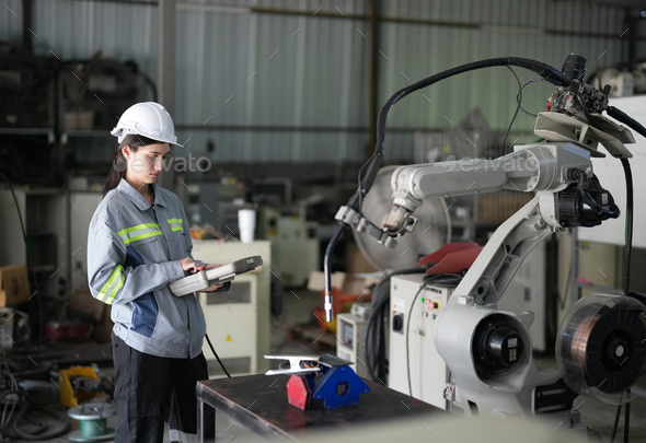 Engineer inspecting automatic AI robot arm and machines in factory ...