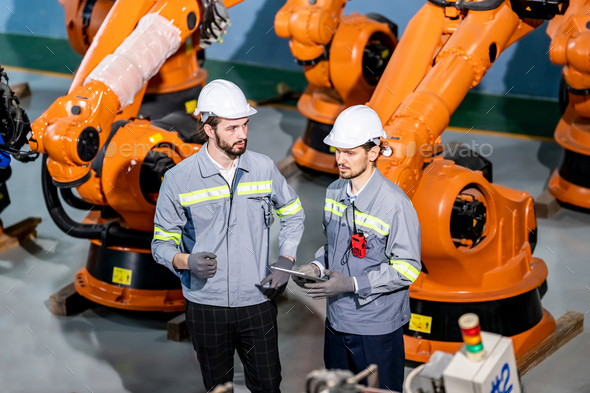 Engineer inspecting automatic AI robot arm and machines in factory ...