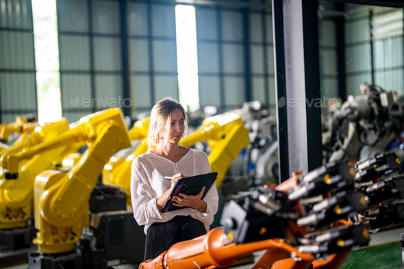 Engineer inspecting automatic AI robot arm and machines in factory ...